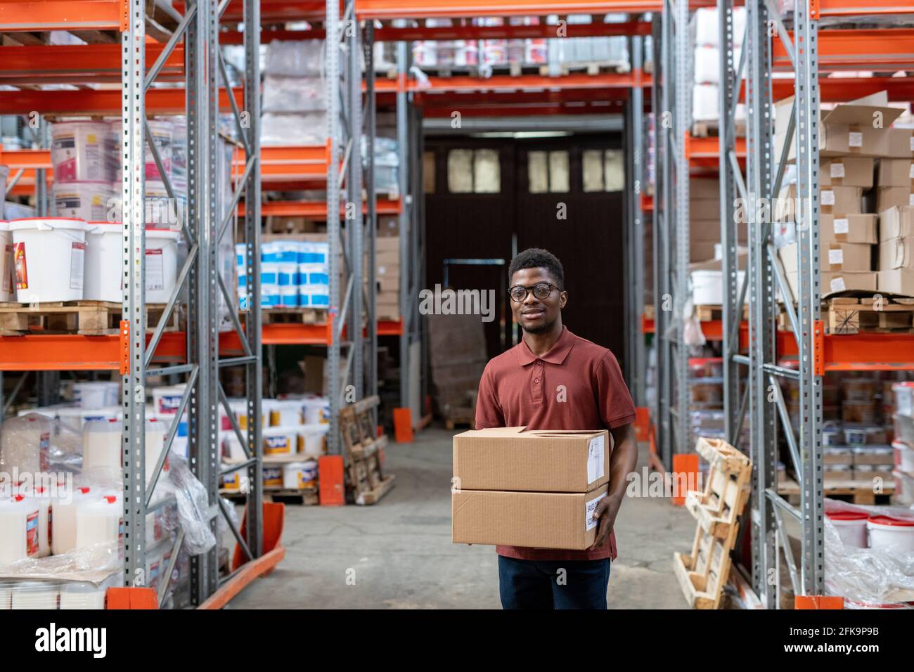 Positive young African-American storeroom worker in glasses walking ...