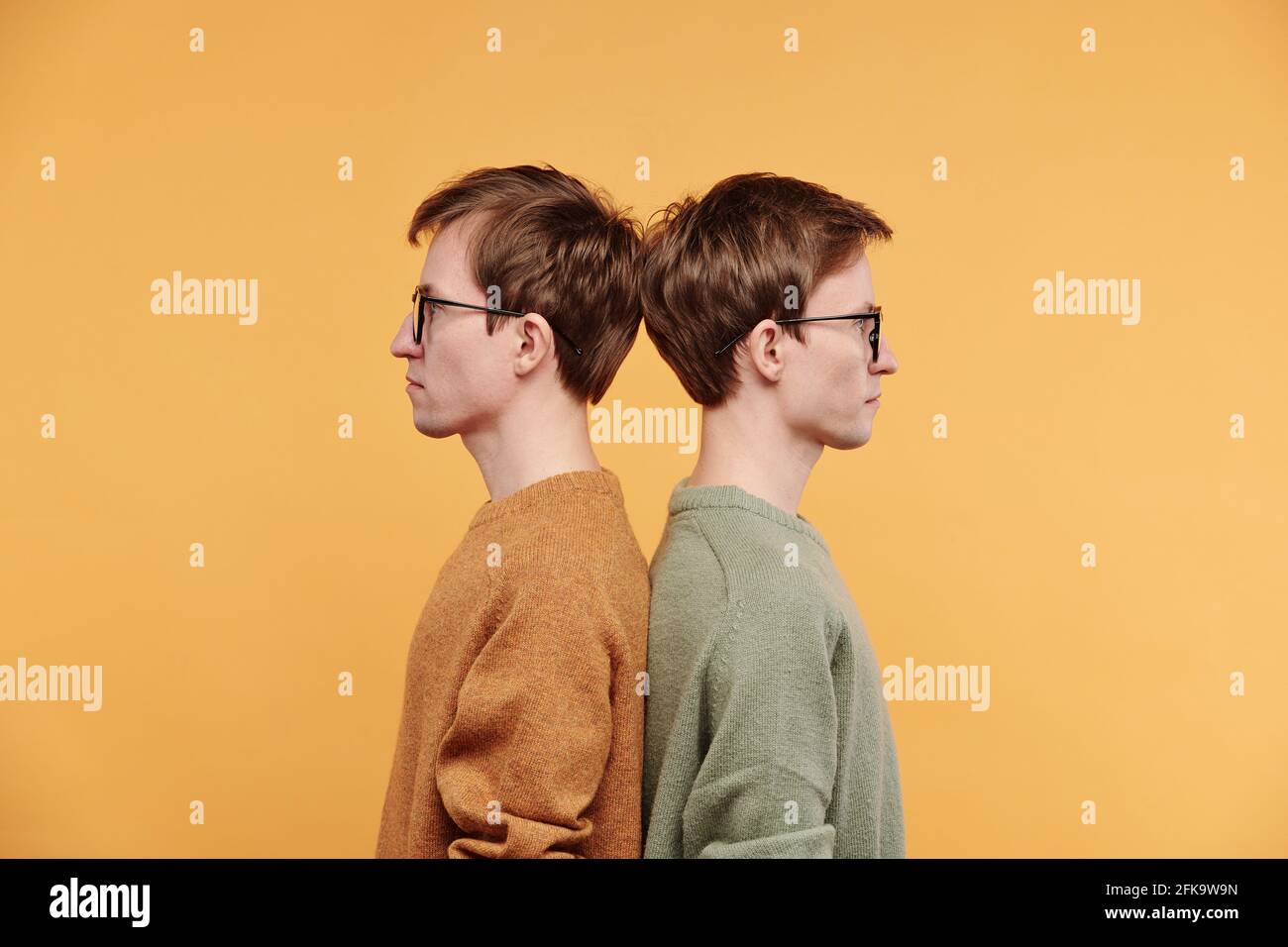 Side view of serious twin men in mustard and olive sweaters standing ...