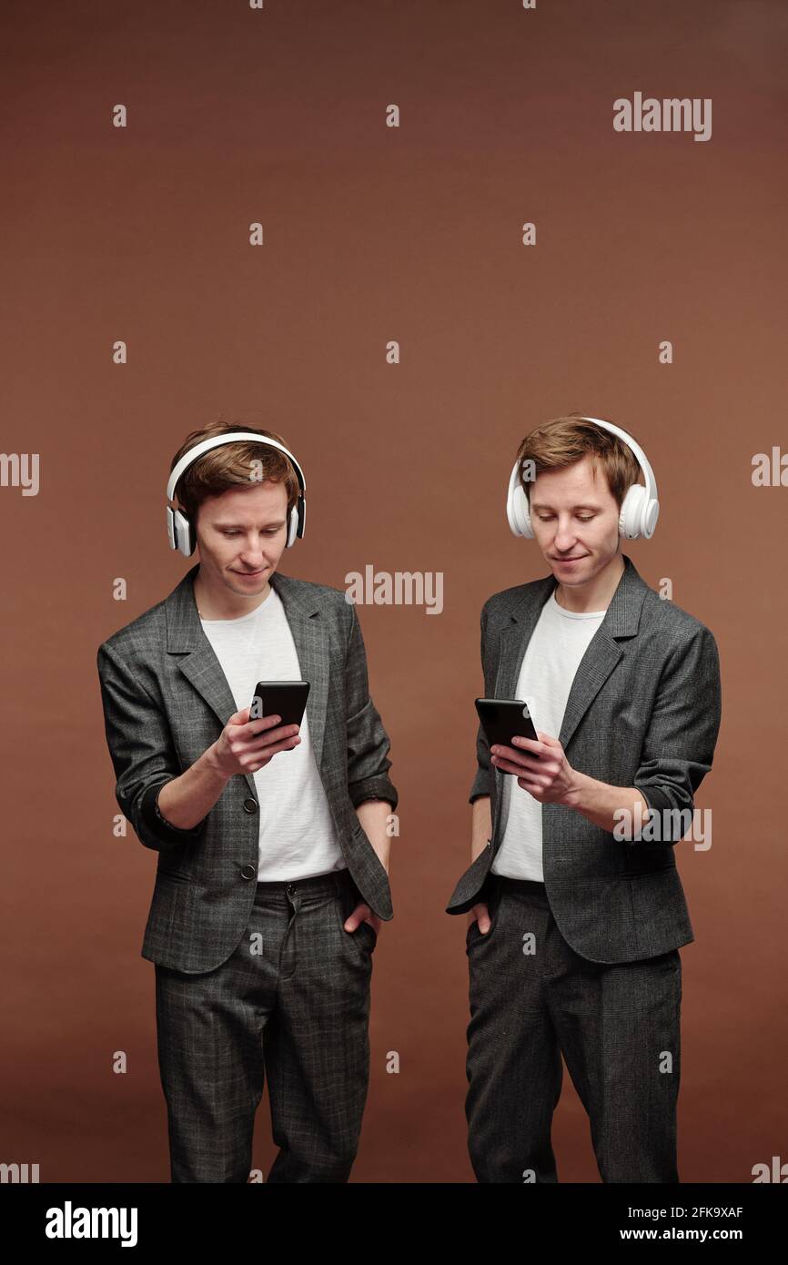 Positive young twin brothers of music lovers standing against brown ...