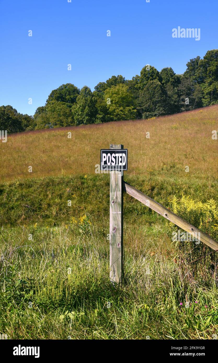 Wooden fence post holds sign warning that the land beyond is private ...