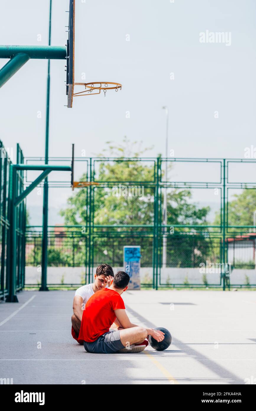 Two strong caucasian athletes resting on the ground at the basketball ...