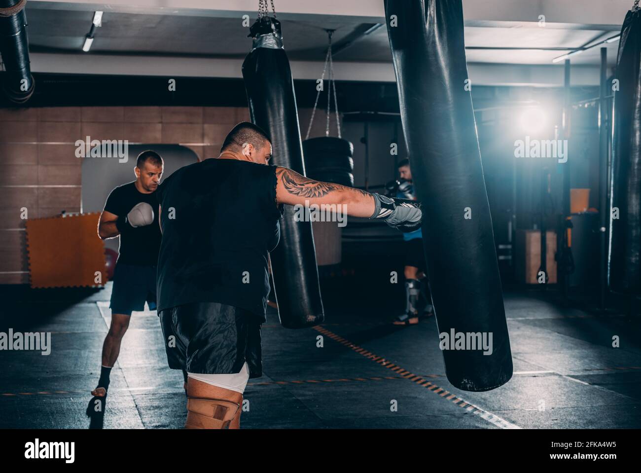Strong kickboxer man punching black sand bag on gym background Stock ...