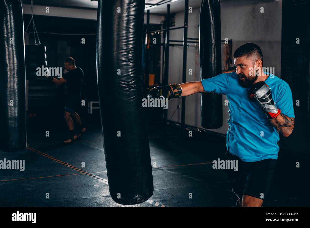 Handsome boxer in boxing gloves training with punching bag on dark ...