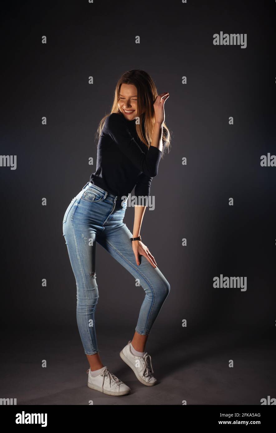 Side full-body portrait of a young female model in black top and jeans ...