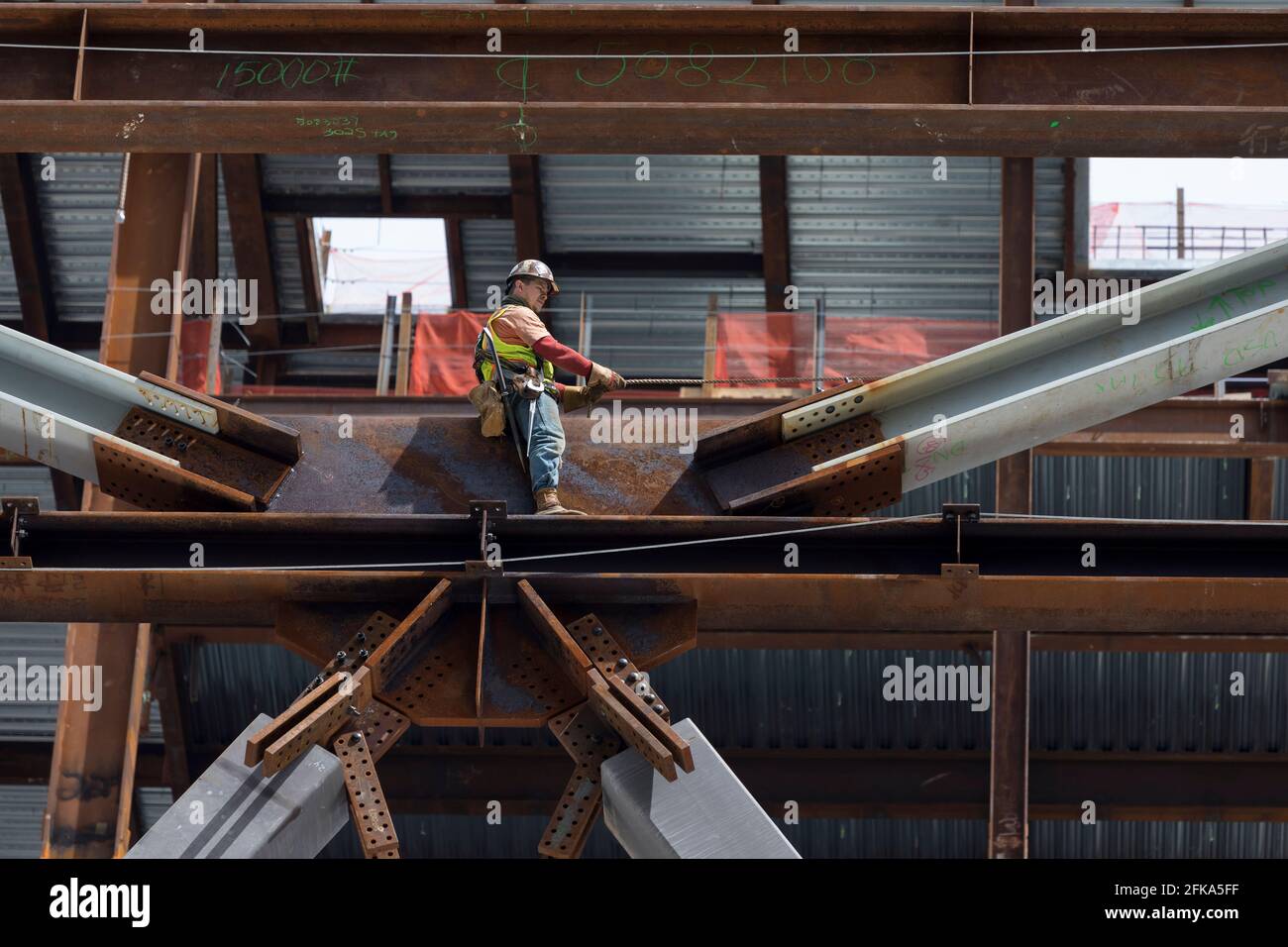 A construction worker helps guide a steel truss into place at the ...