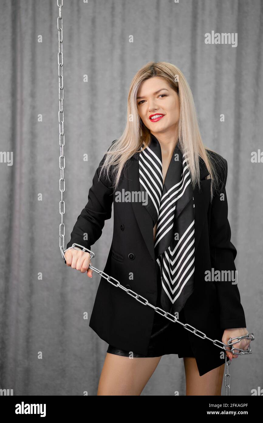 Strong woman in black jacket and leather shorts holds metal chain in ...