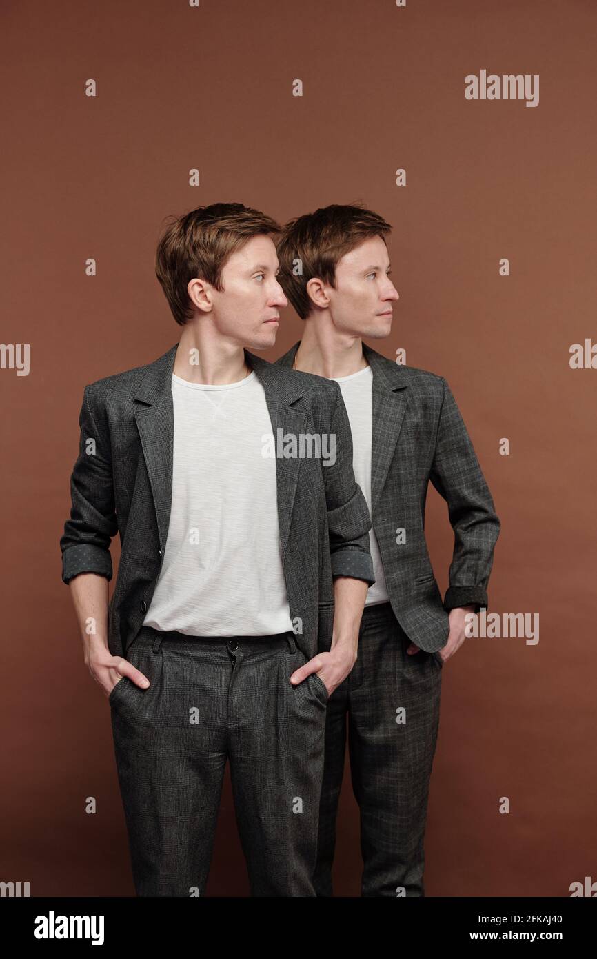 Profile of confident young twin brothers in gray suits standing against ...
