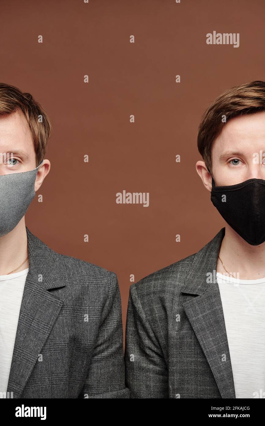 Conceptual photo of young twins in facial masks standing against brown ...