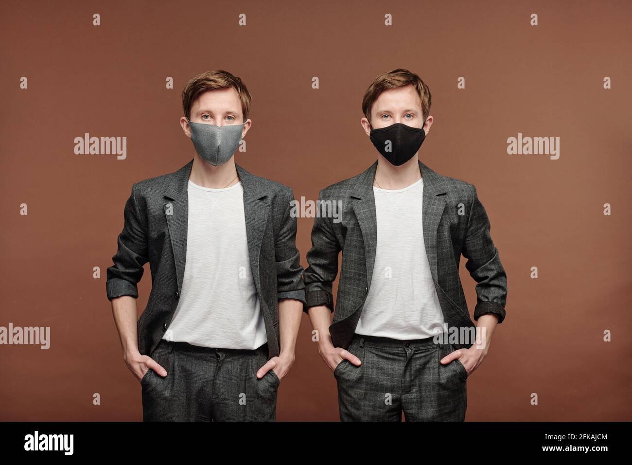 Portrait of handsome young twin brothers in gray suits and cloth mask ...