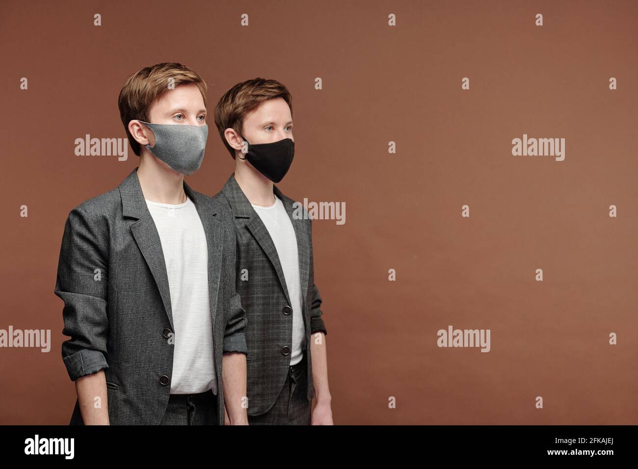 Row of serious young twins in gray suits standing in facial masks ...