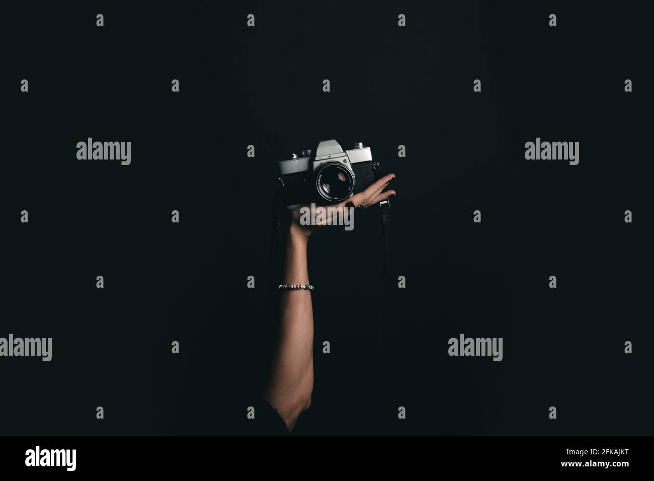 Woman's hand holding an analogue camera in studio with a black backdrop ...