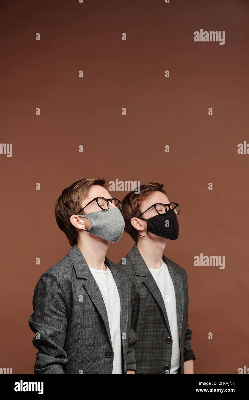 Row of two twin brothers in cloth masks and glasses keeping eyes closed ...