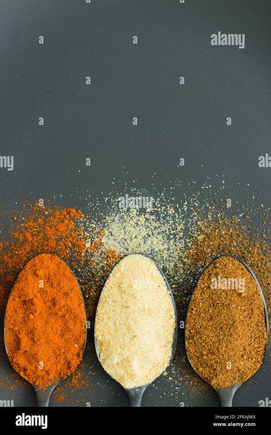 Red, white and brown spices on three black spoons on gray background ...