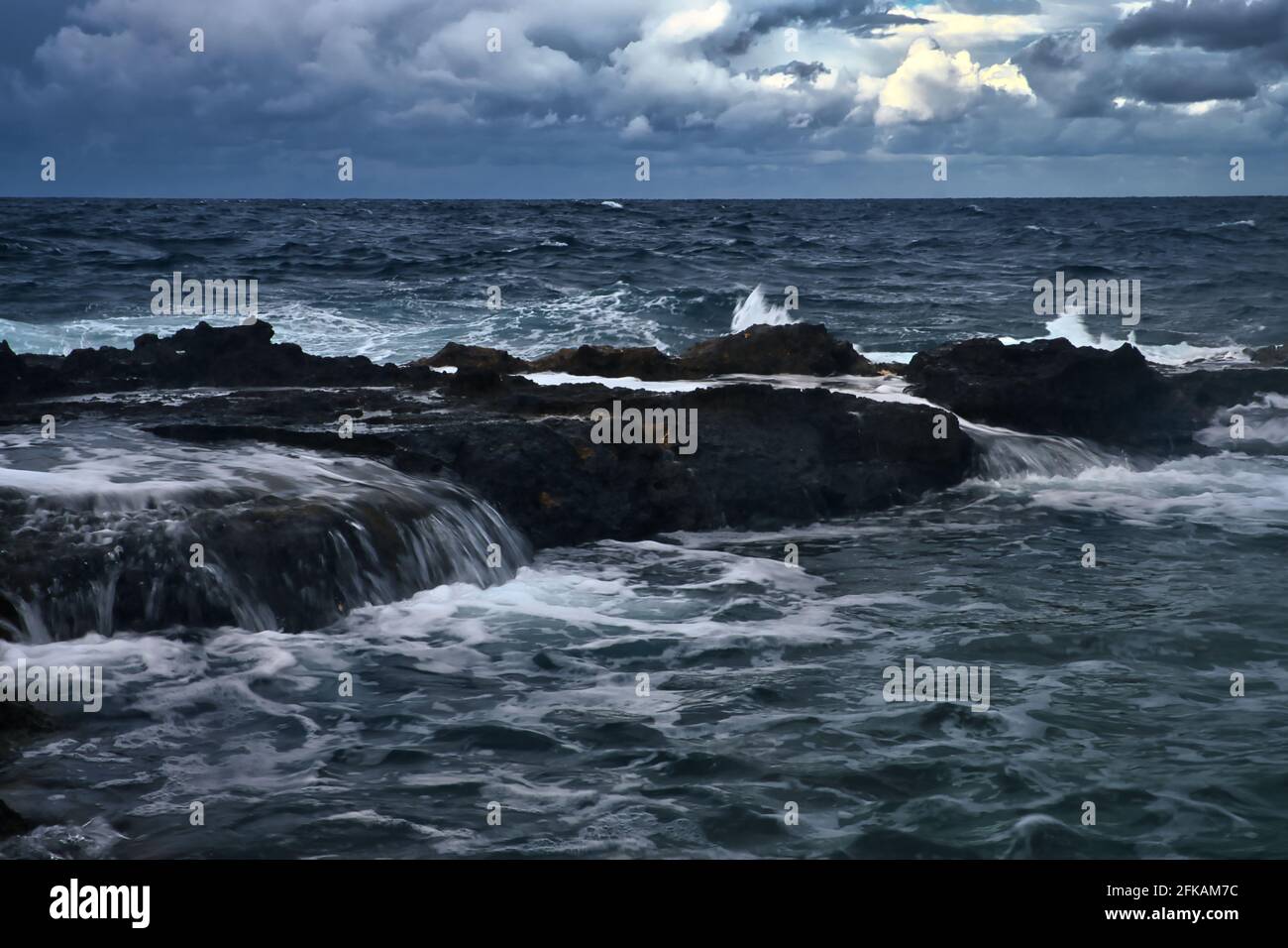 Water running over rocks in the ocean on a dark stormy and cloudy day ...