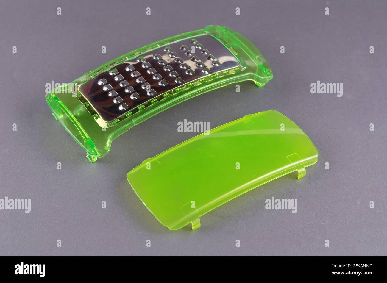 Metal grater with a green plastic protective cover lies on a gray ...