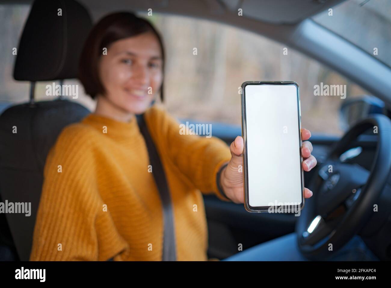 A young happy woman driving a car, she shows empty phone screen ...
