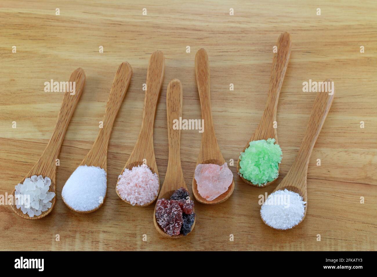 Spoons of commercial salt and natural rock salt on a wooden background ...