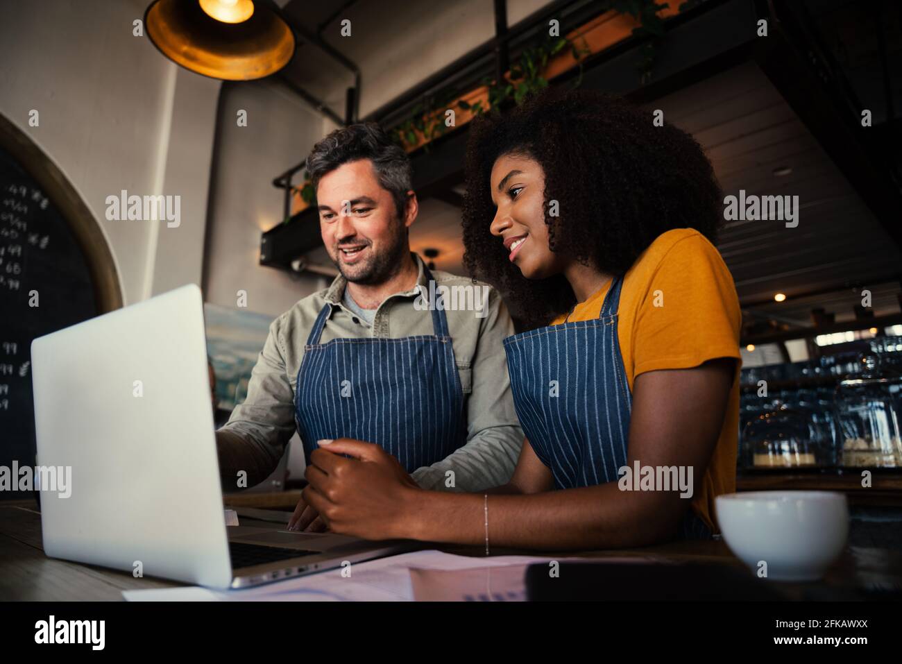 Manager of coffee shop training intern showing menu on laptop while ...