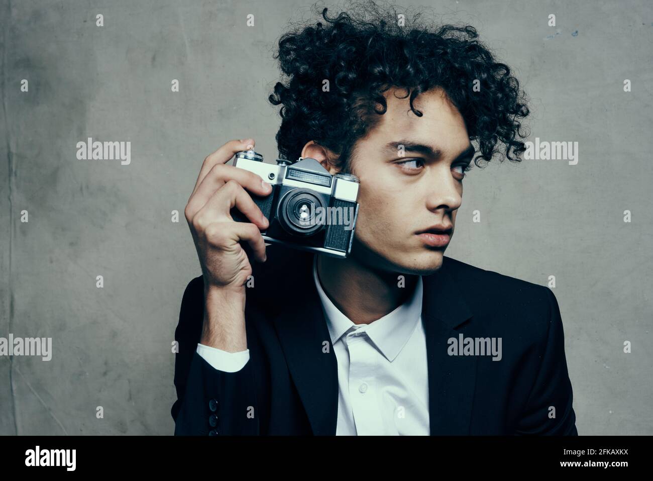curly-haired man in a jacket and shirt holding a camera in his hand ...