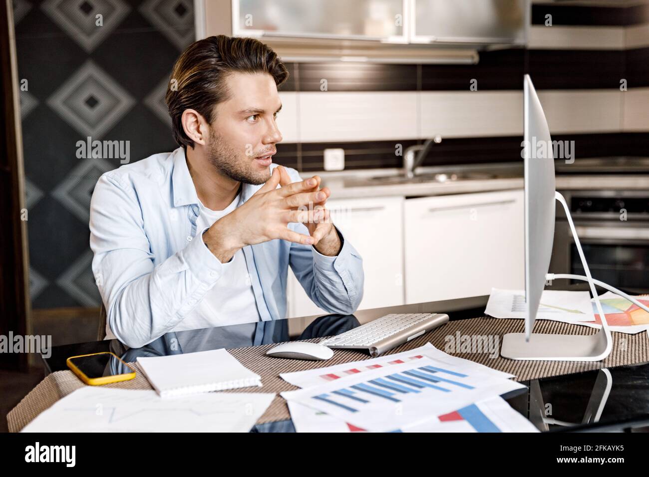 Stylish male employee is sitting at the desk in home office, using ...