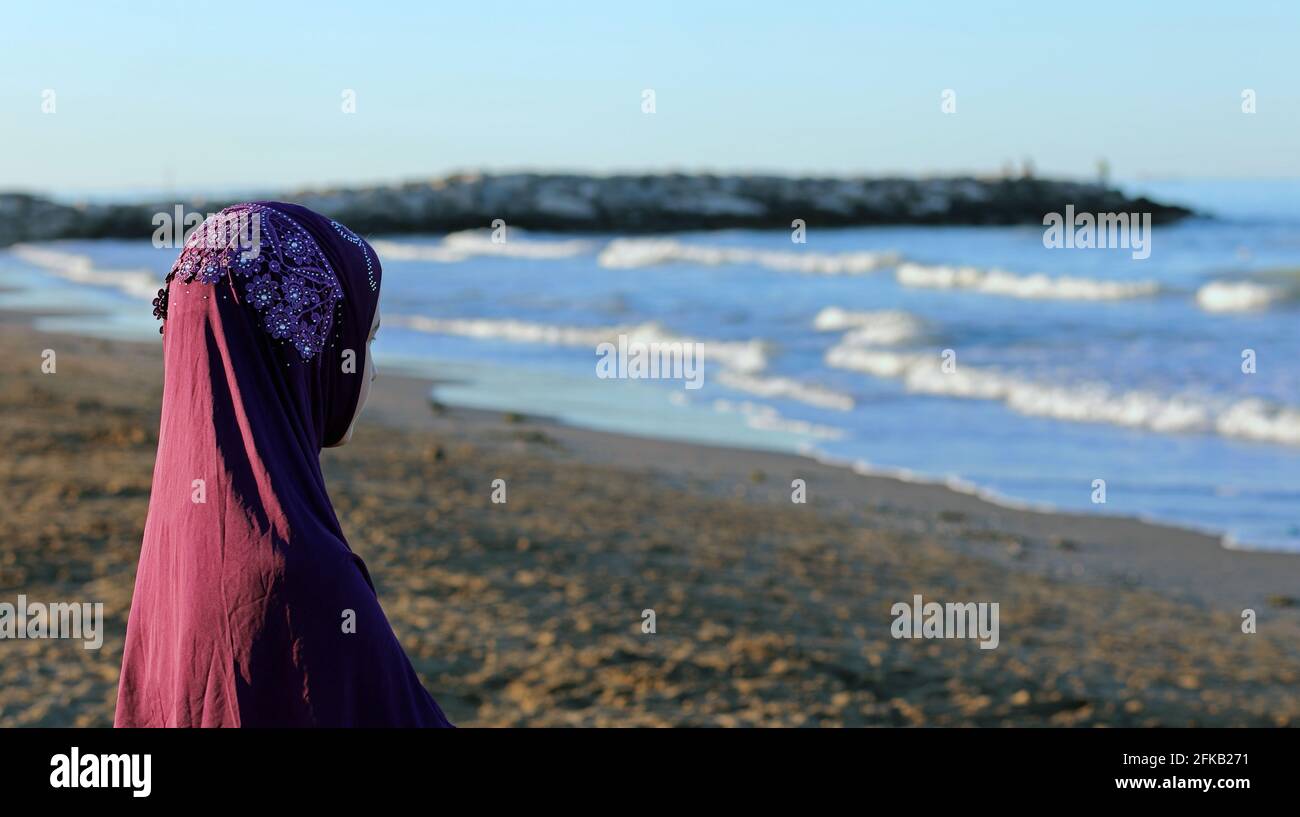 young girl with the Arab veil to cover her head by the sea awaits the ...