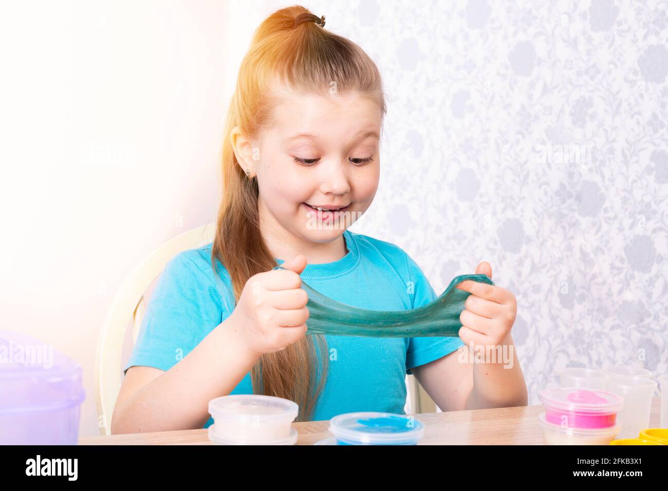 Blond beautiful caucasian little girl is playing with slime and smiling ...