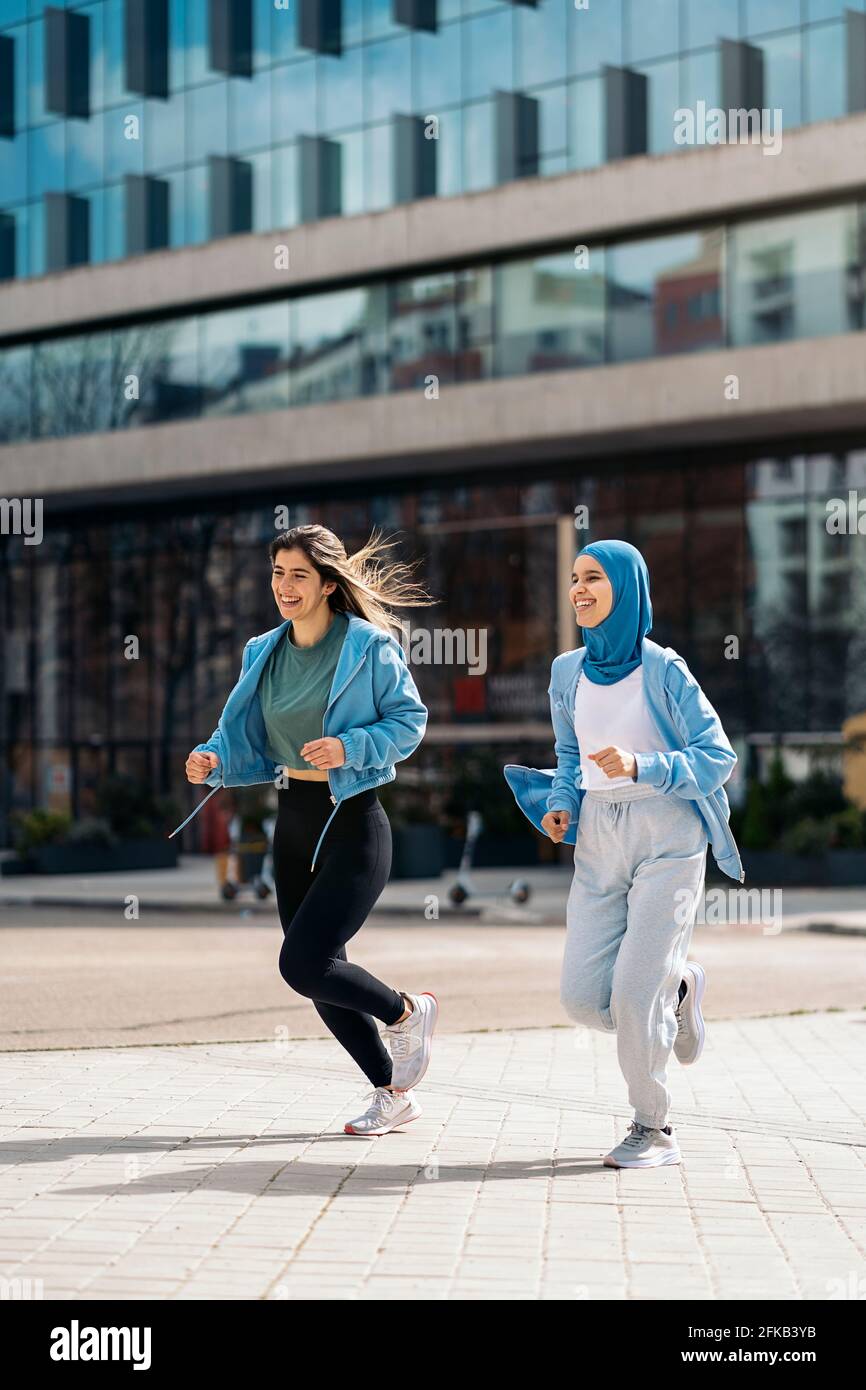 Cheerful muslim woman wearing hijab running in the street with her ...
