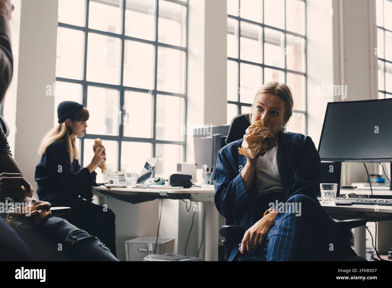 Female entrepreneur eating food while working in office Stock Photo - Alamy