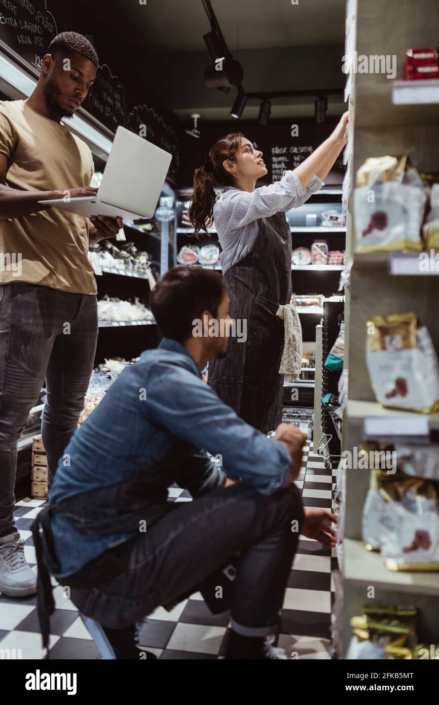 Female owner arranging product on rack while male colleagues working in ...