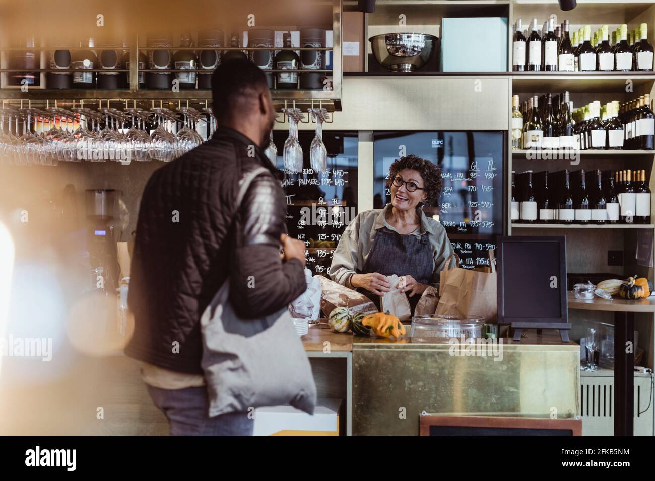 Female store owner talking with male customer while packing order at ...