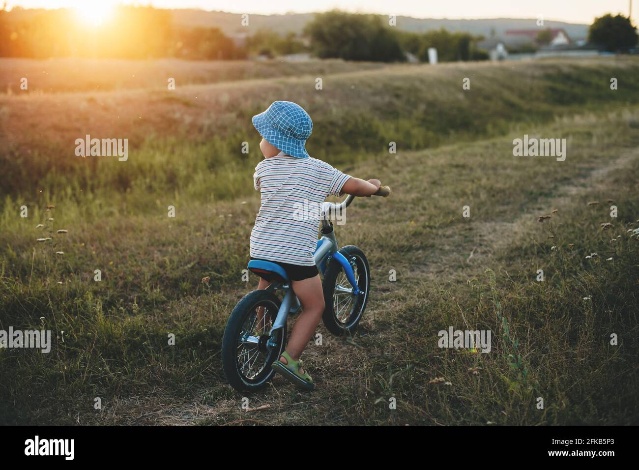 back view photo of a caucasian kid driving the bike in a green field ...