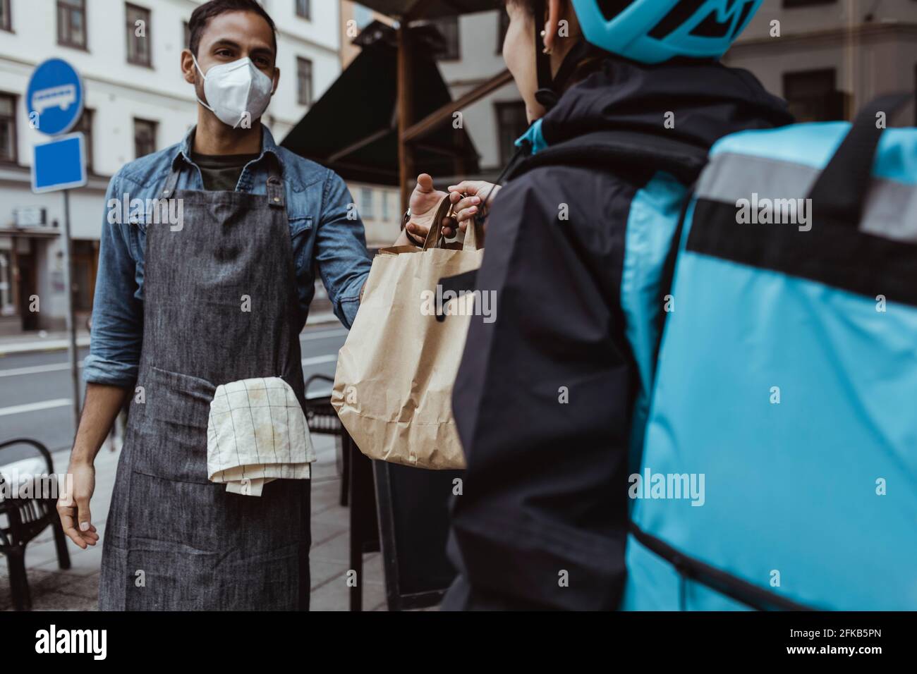 Delivery woman collecting order from male owner on footpath during ...