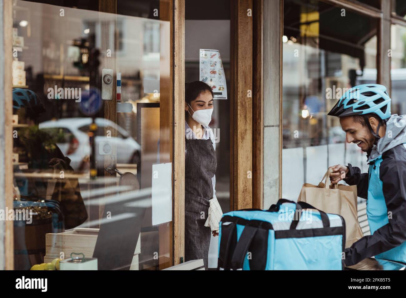 Smiling delivery man collecting order from female owner at delicatessen ...