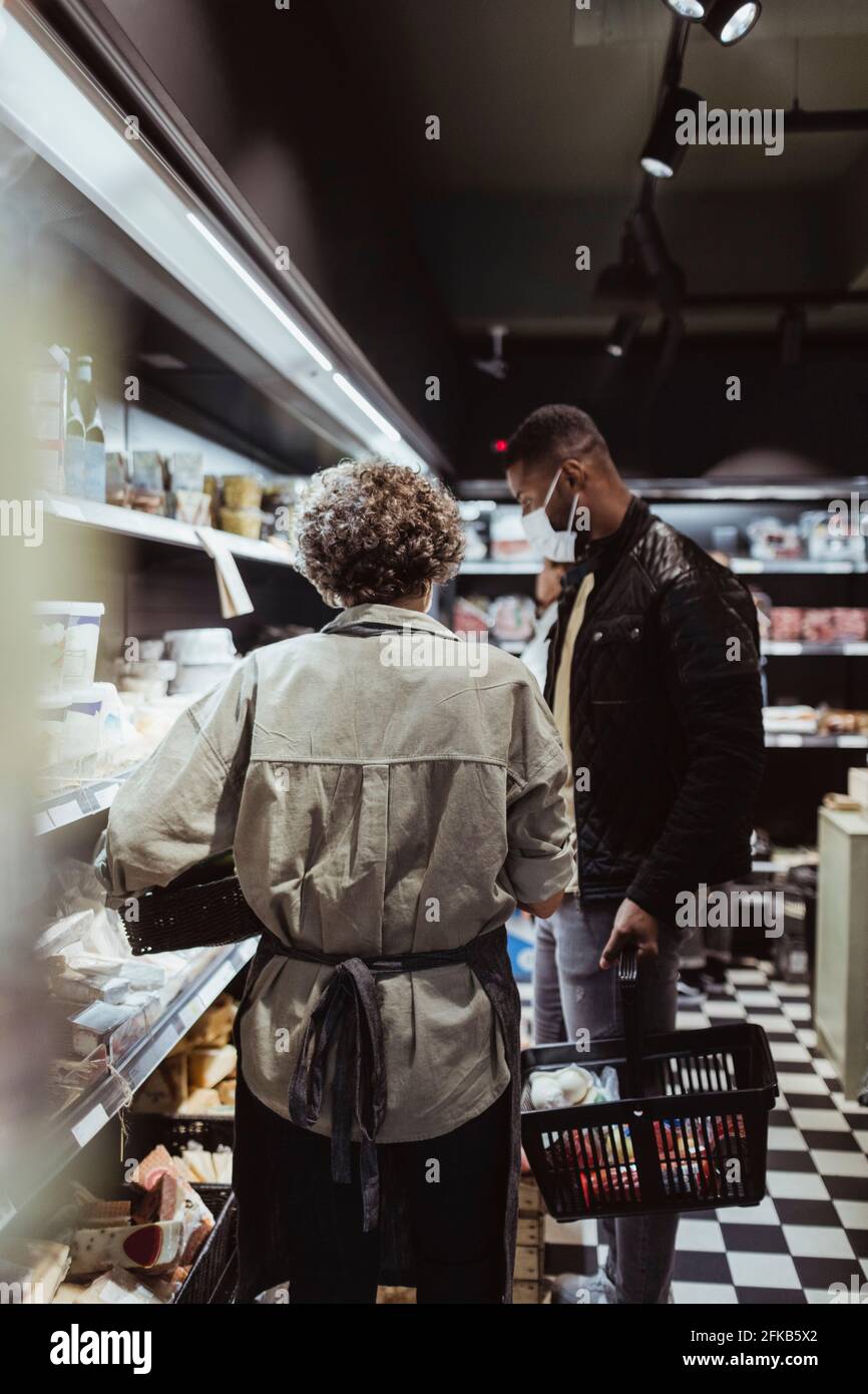 Male customer with food basket standing by female owner in store during ...