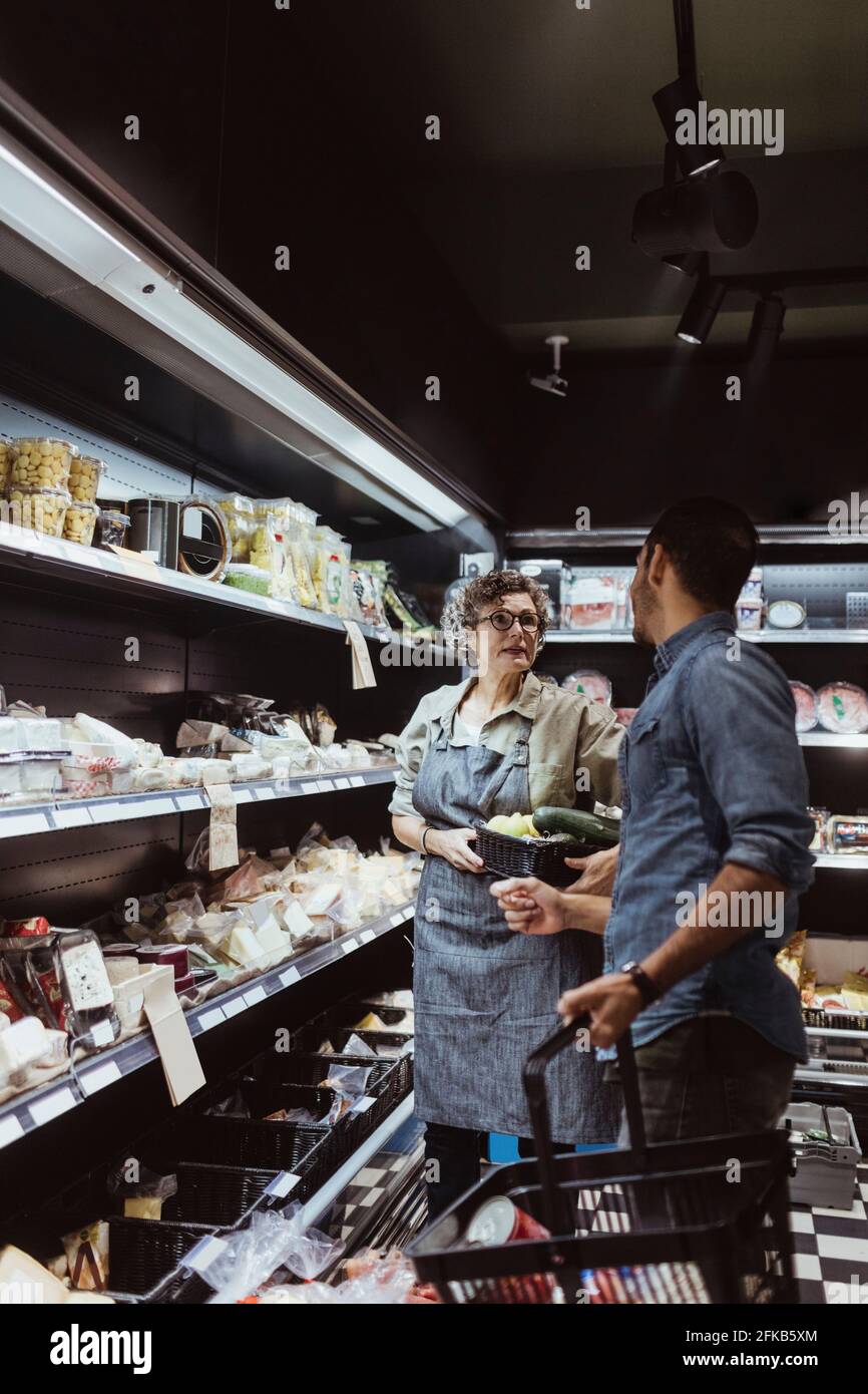 Female store owner talking with male customer at delicatessen shop ...
