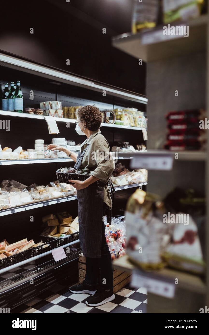 Female owner arranging food product on rack at deli shop during ...