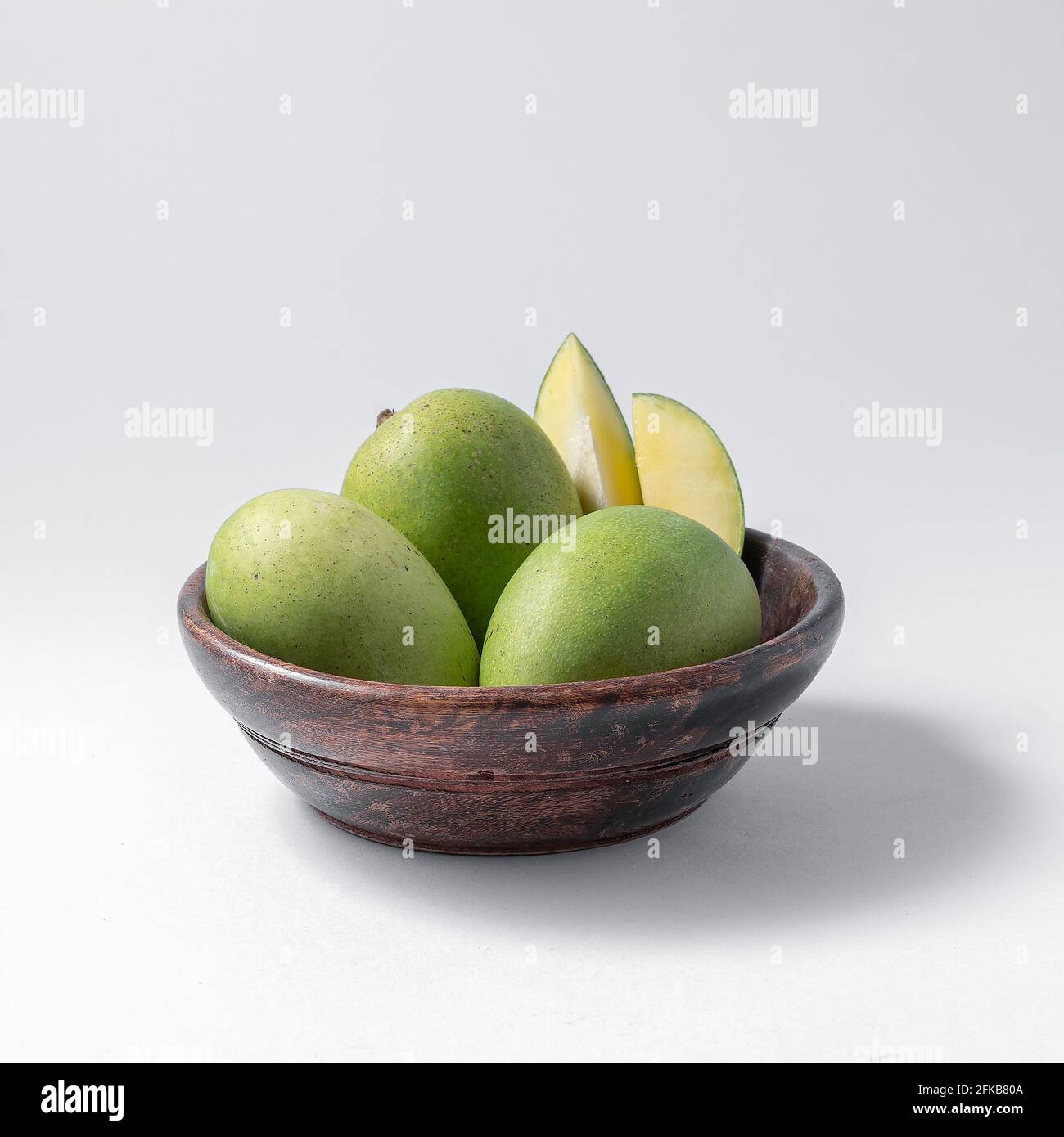 raw mangos or aam or kairi or tropical fruits in a wooden bowl on white ...