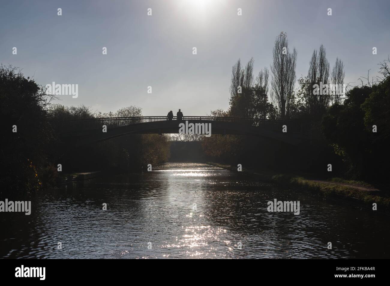 Silhouettes of a couple walking over a bridge on the Grand Union Canal ...
