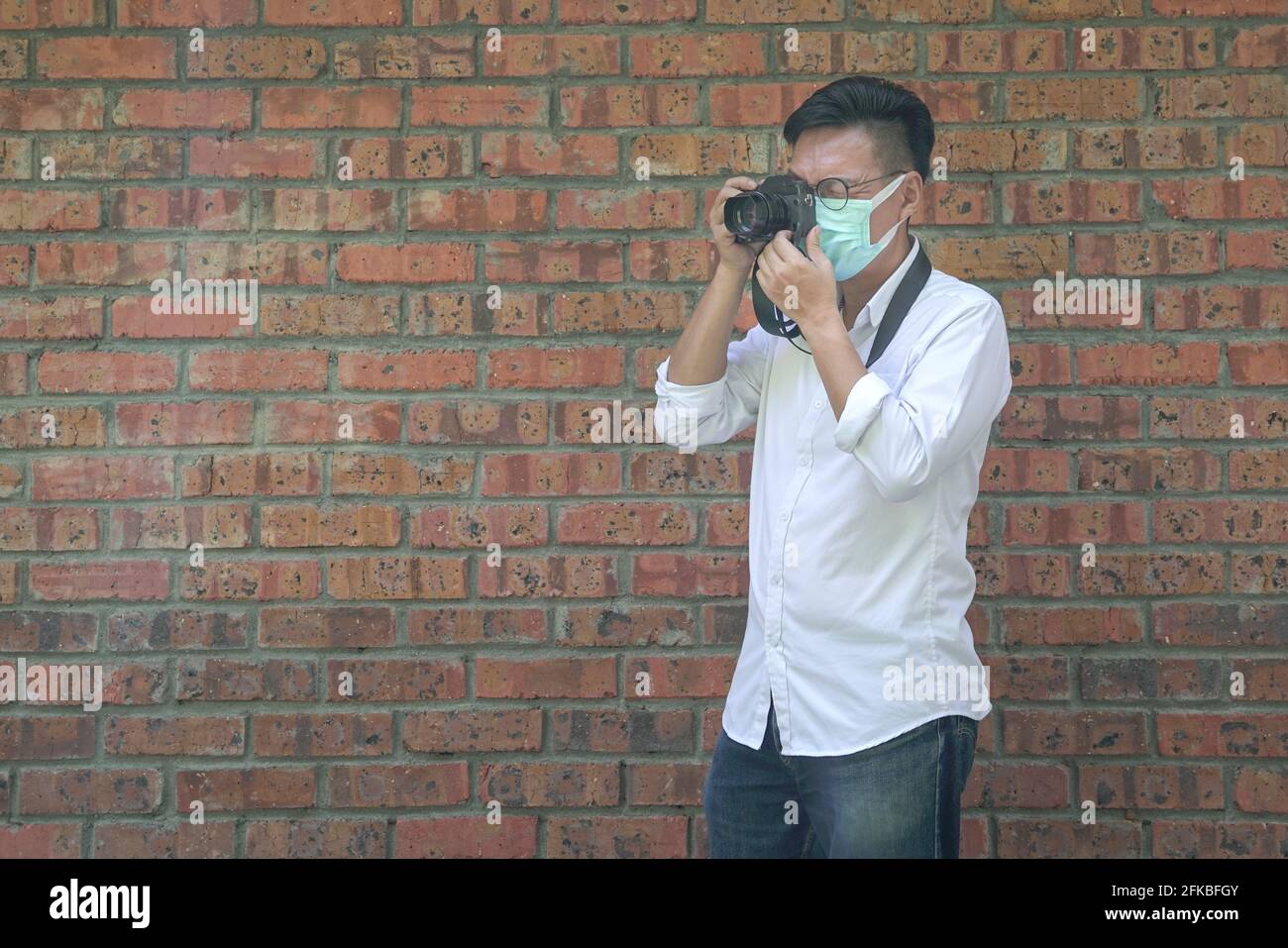 Male photographer wearing face mask in white shirt and jeans. Brick ...