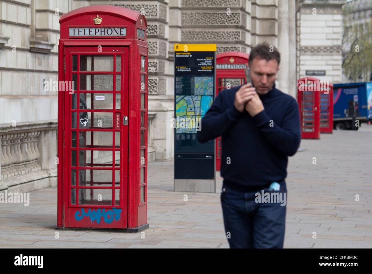 Person on mobile phone while walking past red telephone boxes kiosks in ...