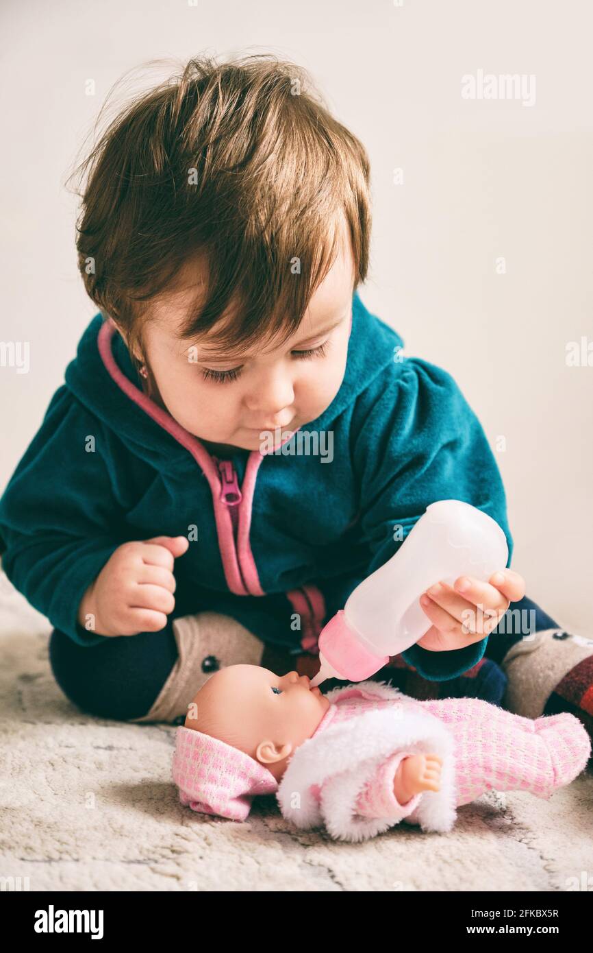 Baby girl playing with a doll, feeding a doll from a bottle, taking ...