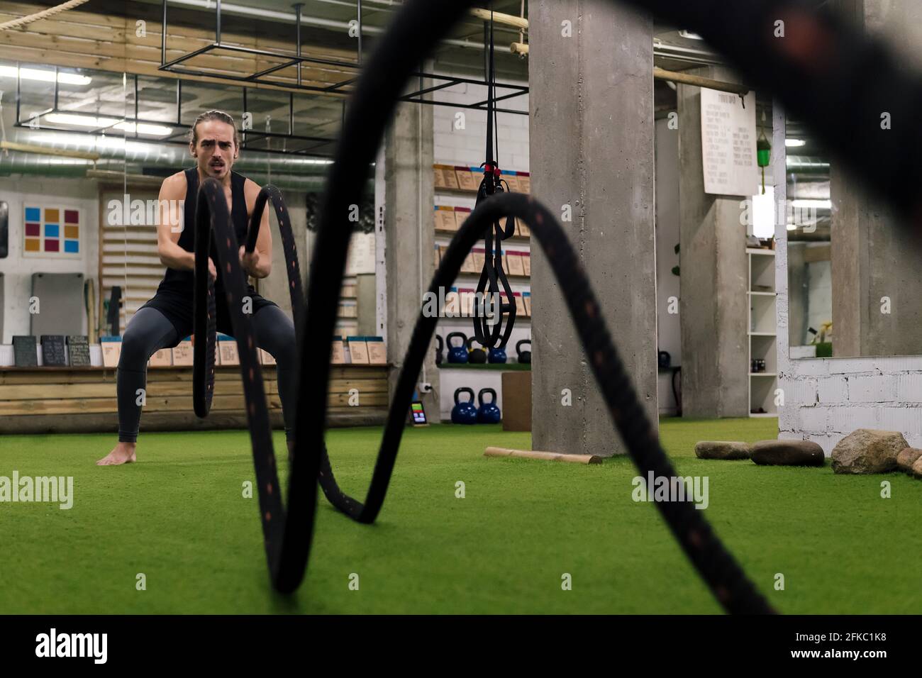 sportsman doing functional training by shaking the ropes in the gym ...