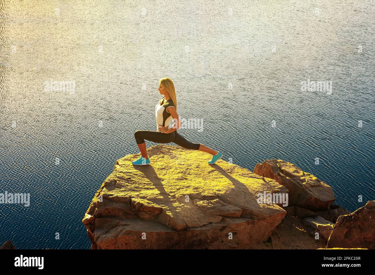 Young slim woman practicing yoga outdoors on stone shore of mountain ...