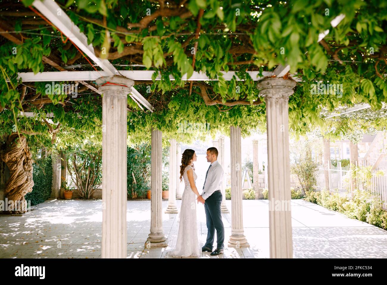 Happy bride and groom holding hands stand between columns in a ...