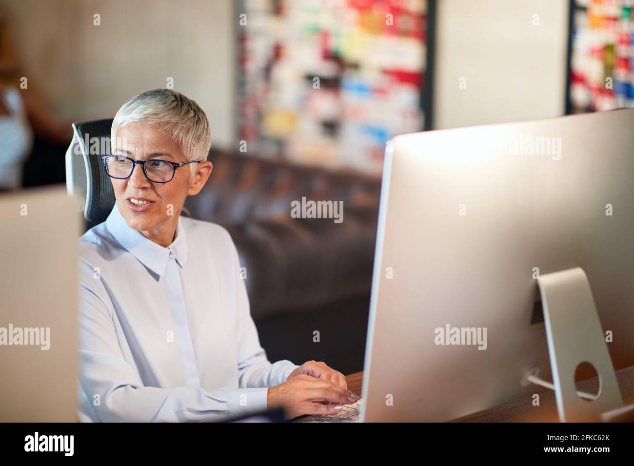 An elderly business woman sitting and working at a desk in a working ...