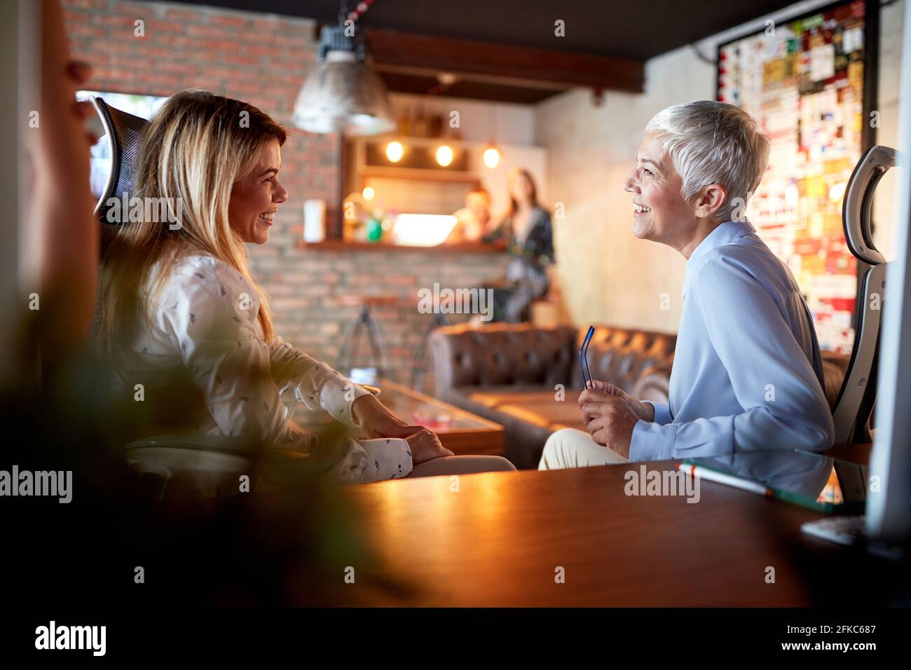 Young happy woman being mentored by female senior partner in the office ...