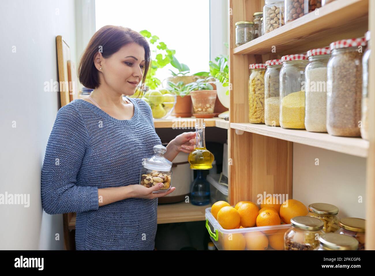 Organization of pantry, woman in kitchen near wooden rack with cans and ...
