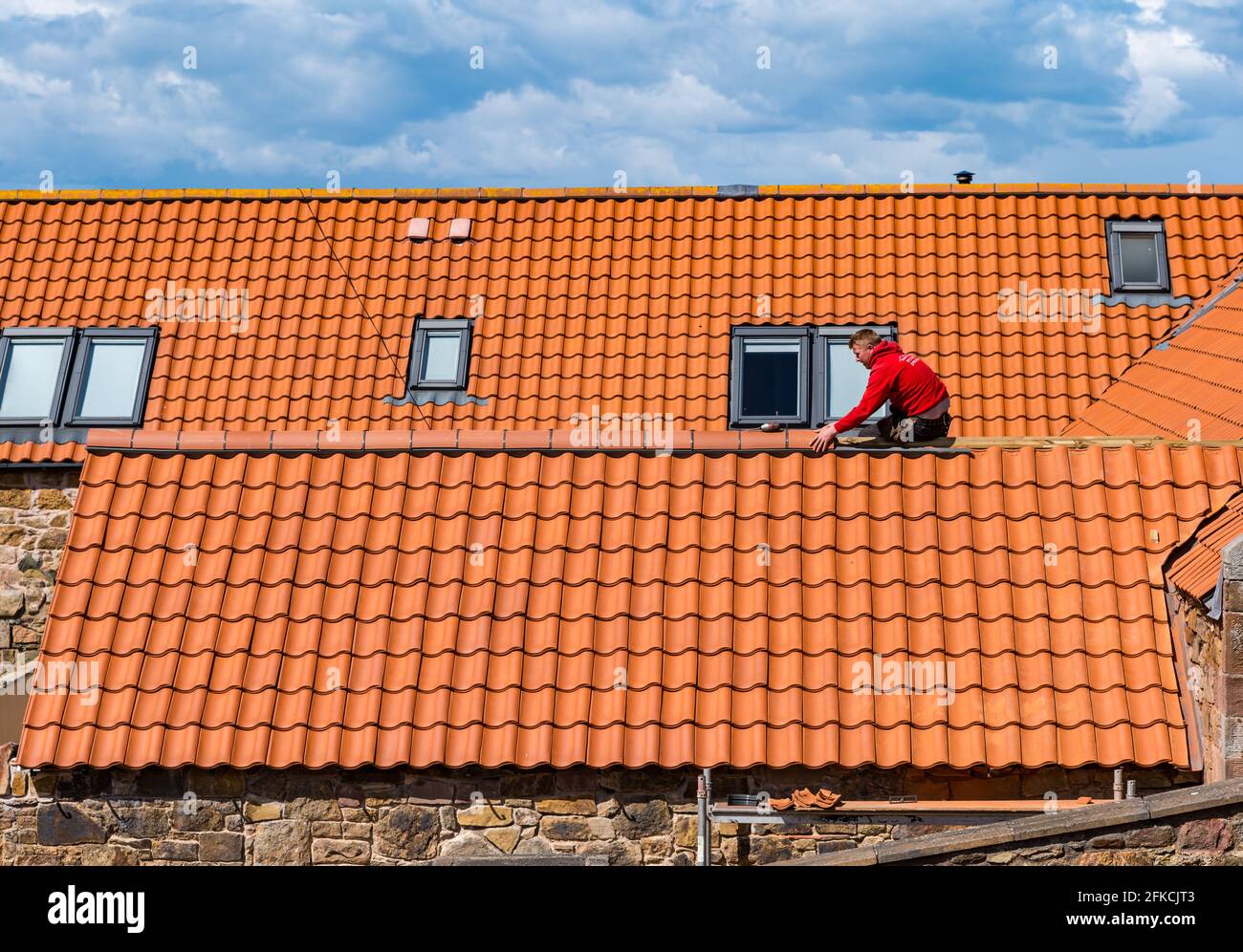 Workman roofer laying red tiles on roof of old farm building house ...