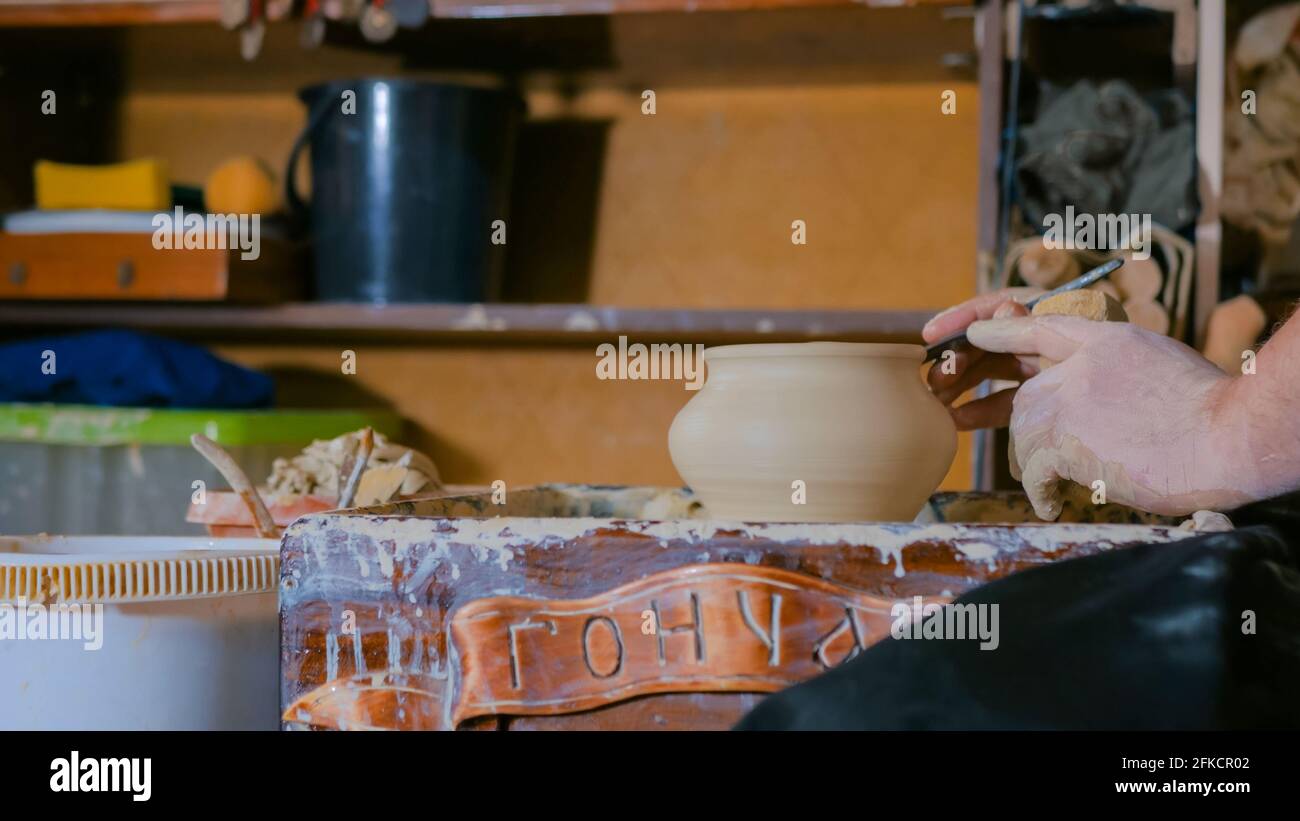 Professional potter carving pot with special tool in pottery workshop ...