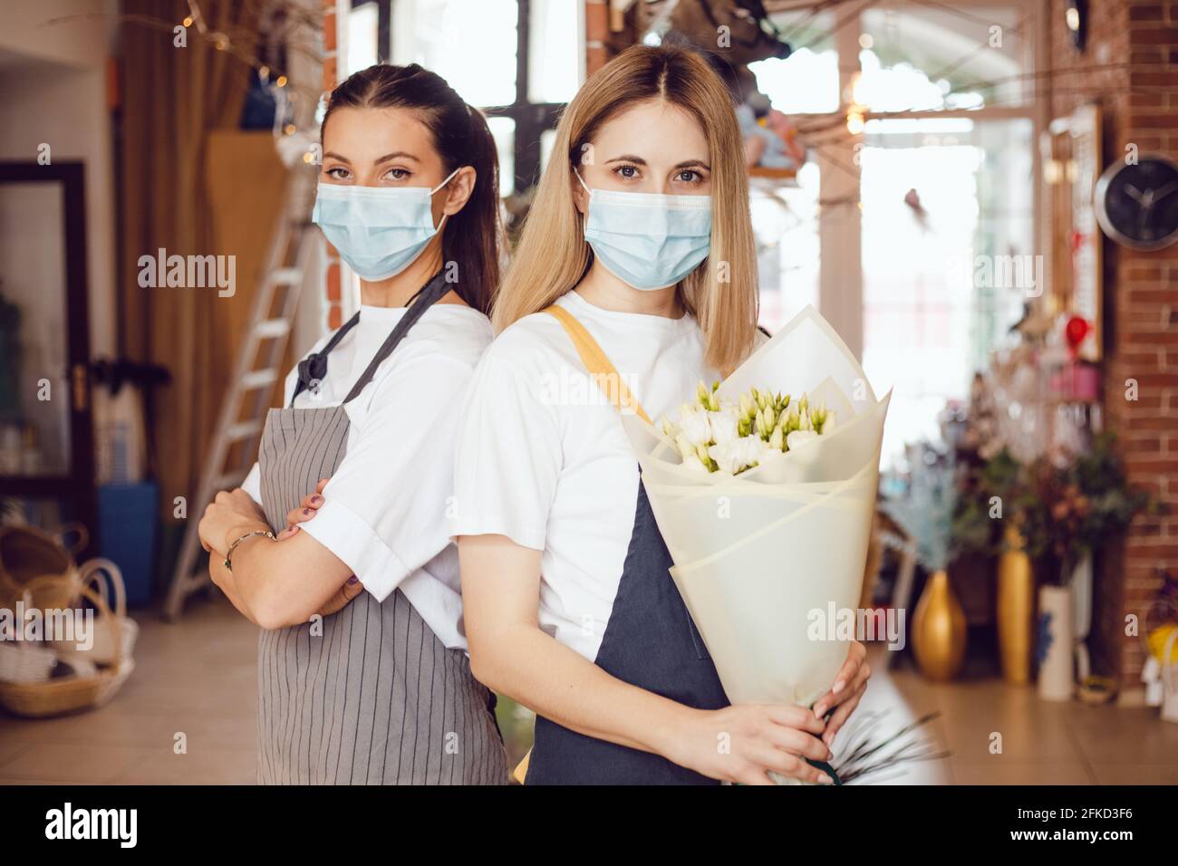 Florist girls in medical masks with a bouquet in their hands stand in a ...